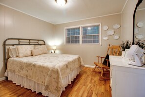 Quarto com cama, poltrona, escrivaninha com computador, janela e detalhes na parede.