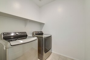 Uma lavanderia com duas máquinas de aço inoxidável, uma prateleira na parede e piso de azulejos brancos.