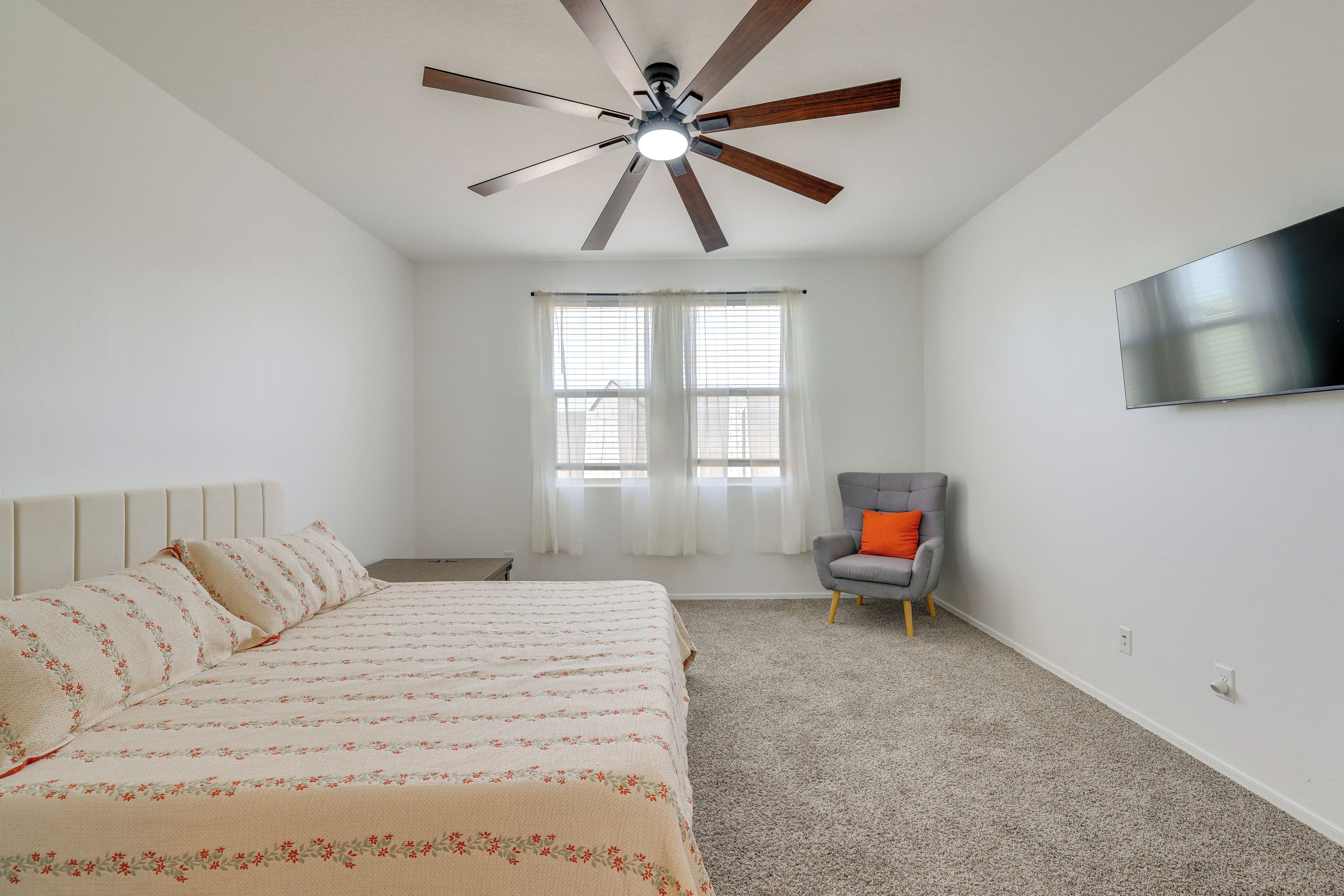 Quarto com cama, poltrona, ventilador de teto e janela com cortinas.
