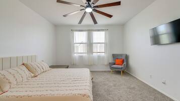 Quarto com cama, poltrona, ventilador de teto e janela com cortinas.