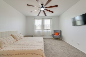 Quarto com cama, poltrona, ventilador de teto e janela com cortinas.