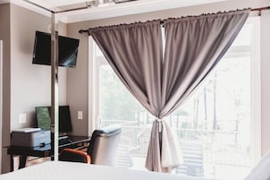 Quarto de hotel com cama, escrivaninha com computador, cadeira e televisão fixada na parede.