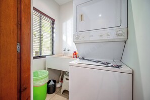 Uma lavanderia compacta com máquina de lavar, pia e janela com persianas.