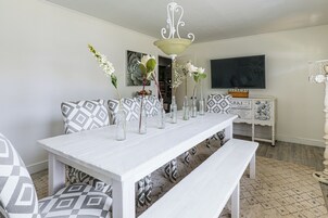 Uma sala de jantar com mesa branca, almofadas estampadas e um banco.