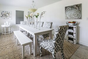 Uma área de refeições com uma mesa branca, cadeiras estampadas e um vaso decorativo como centro.