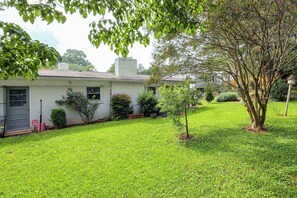 Um imóvel residencial com gramado bem cuidado, uma árvore pequena e uma casa branca com chaminé.