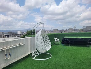 Terraço com grama sintética, uma cadeira suspensa branca e mesa de bilhar.