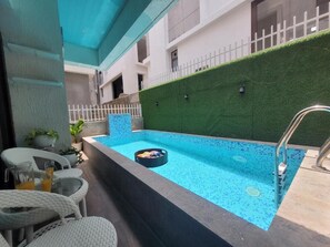 Piscina com cerca branca e grama sintética, rodeada por móveis de vime branco e plantas em vasos.