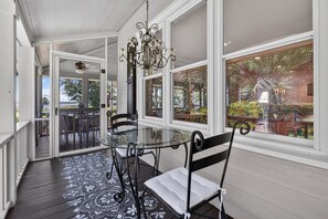 Alpendre coberto com mesa e cadeiras de vidro, um candelabro e vista para um jardim.