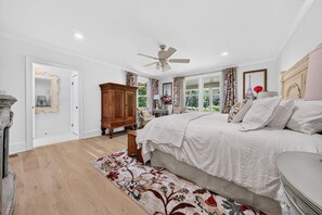 Quarto com cama grande, ventoinha no teto, armário de madeira e vista para o verde pela janela.