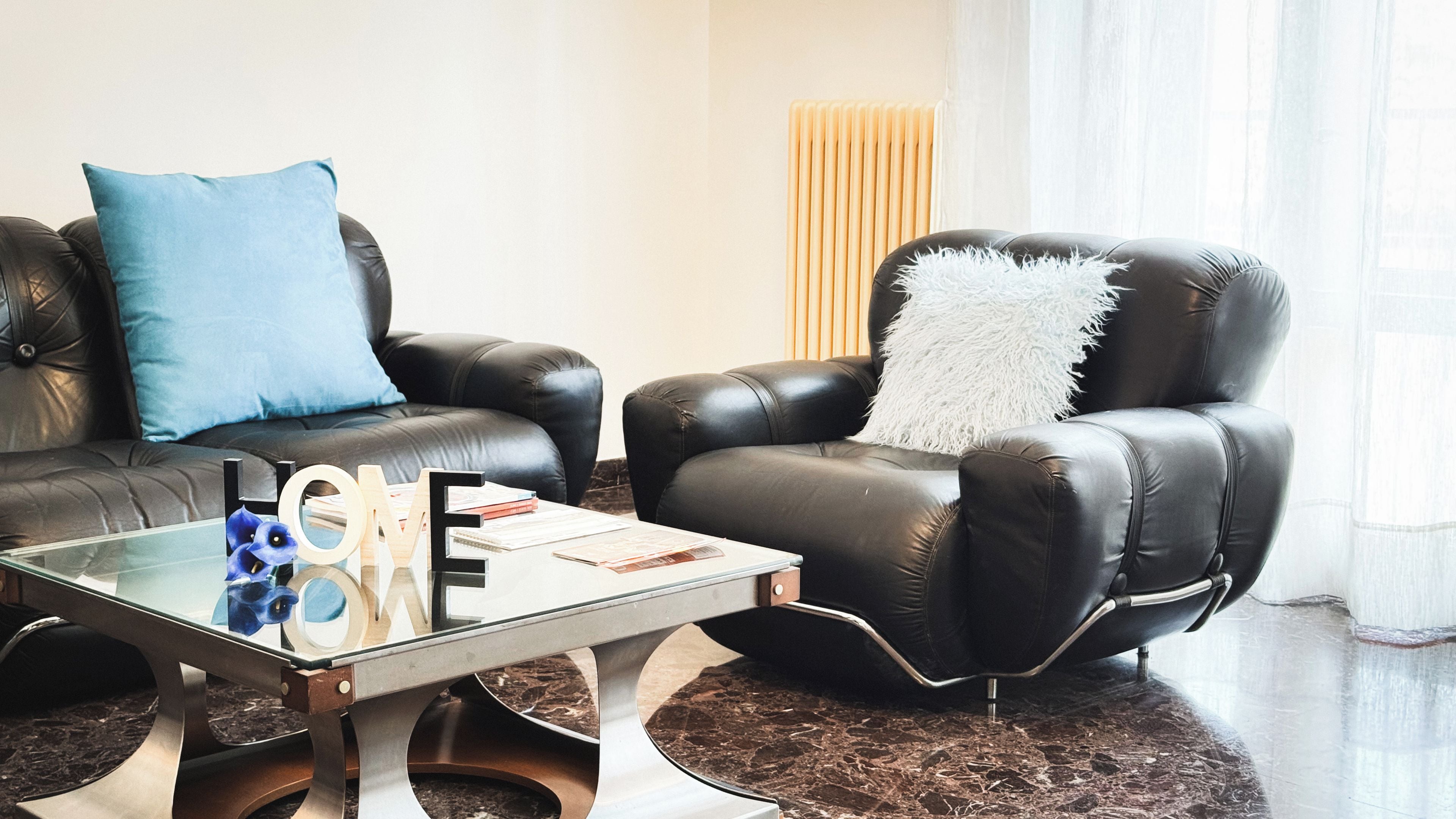 Uma sala de estar moderna com um sofá e uma poltrona de couro preto, e uma mesa de centro de vidro com um objeto decorativo.