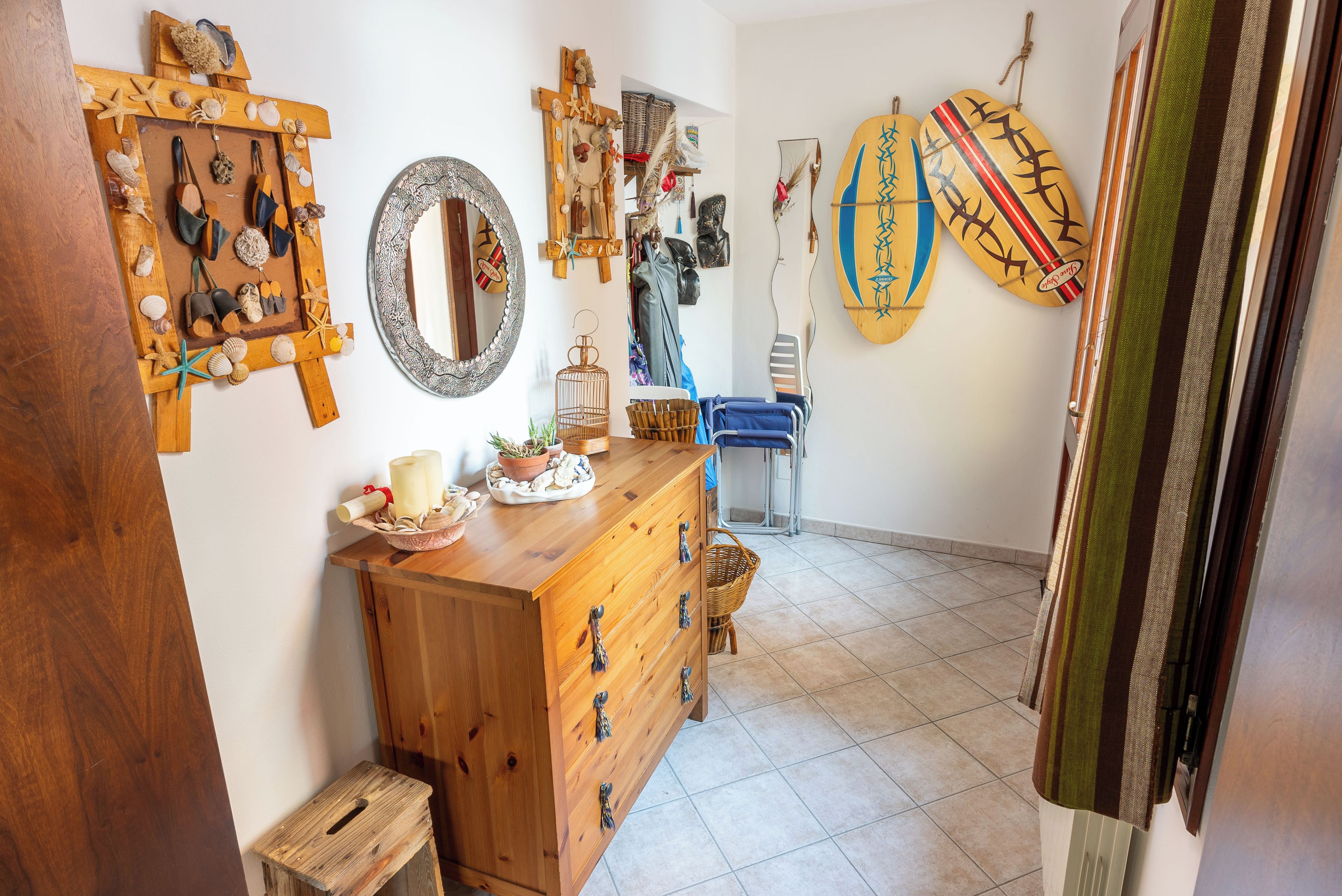 Quarto com cômoda de madeira, espelho e diversos objetos decorativos, incluindo conchas e uma prancha de surf.