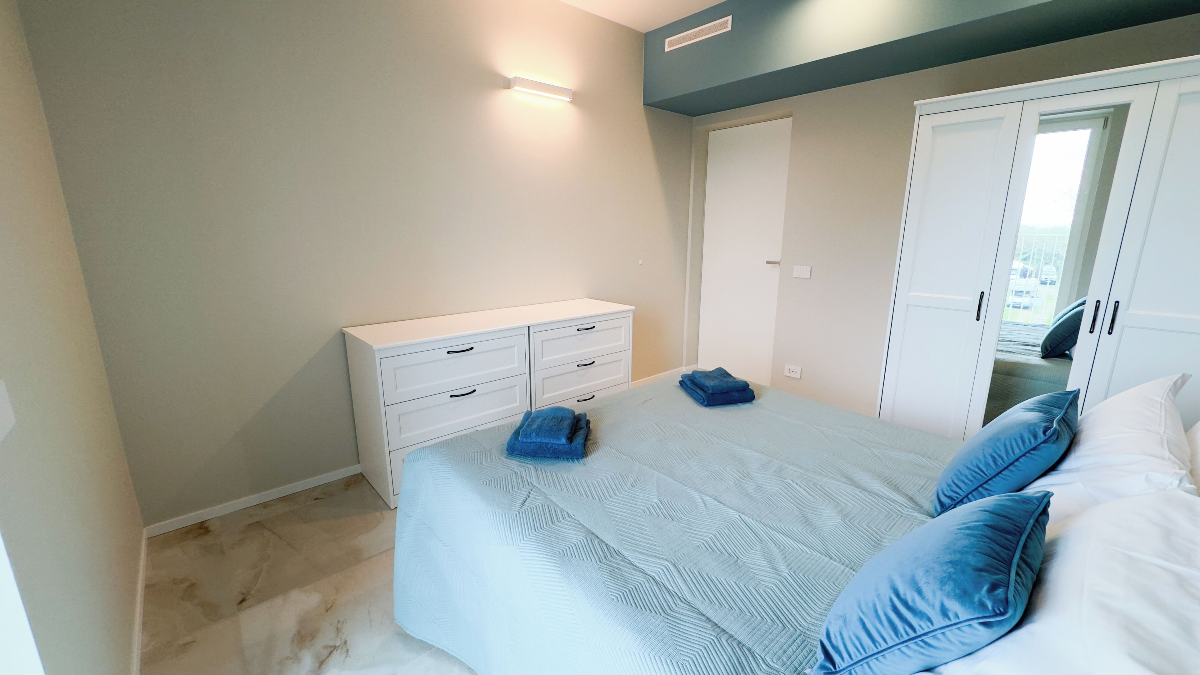 Quarto com cama, cómoda branca e guarda-roupa.