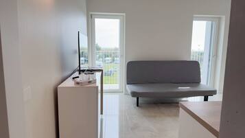 Uma sala de estar moderna com um sofá cinzento, uma televisão de tela plana e uma pequena mesa com um estojo de lenços.