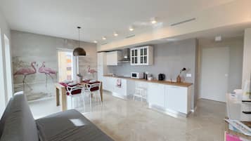 Cozinha moderna com armários brancos, área de refeições com mesa posta para dois e um mural de flamingos na parede.