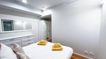 Quarto com cama, guarda-roupa, espelho e banheiro visível por uma porta aberta.