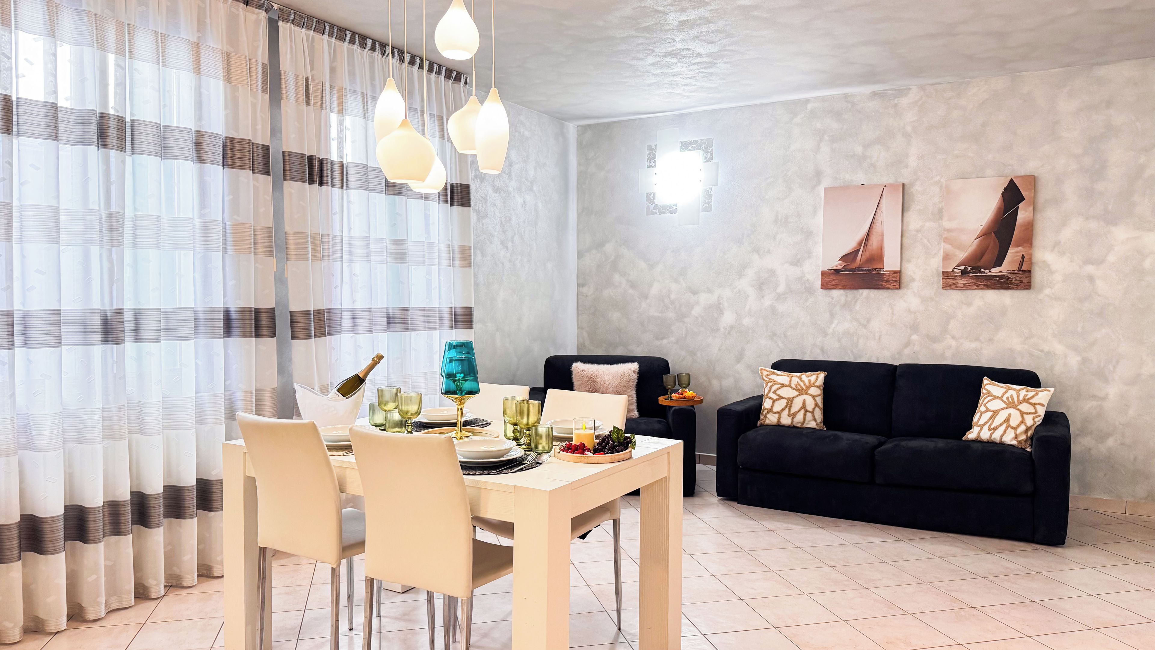 Uma área de refeições com uma mesa posta para dois, um sofá preto e uma parede com duas molduras.