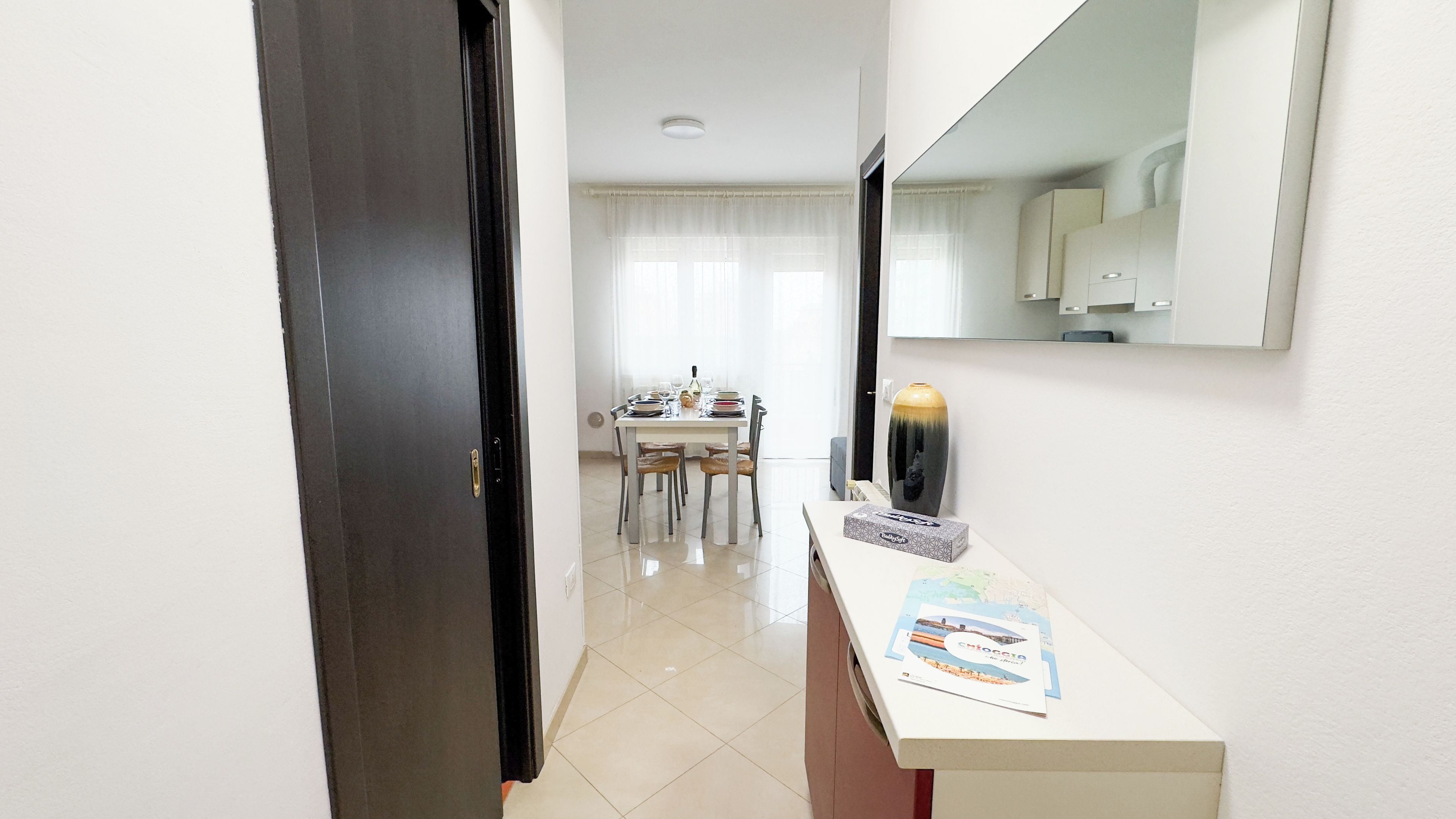 Corredor de hotel com área de refeições ao fundo, uma receção branca e um espelho grande na parede.