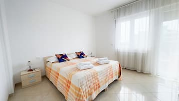Quarto de hotel com cama, mesa de cabeceira, abajur e janela com cortinas.