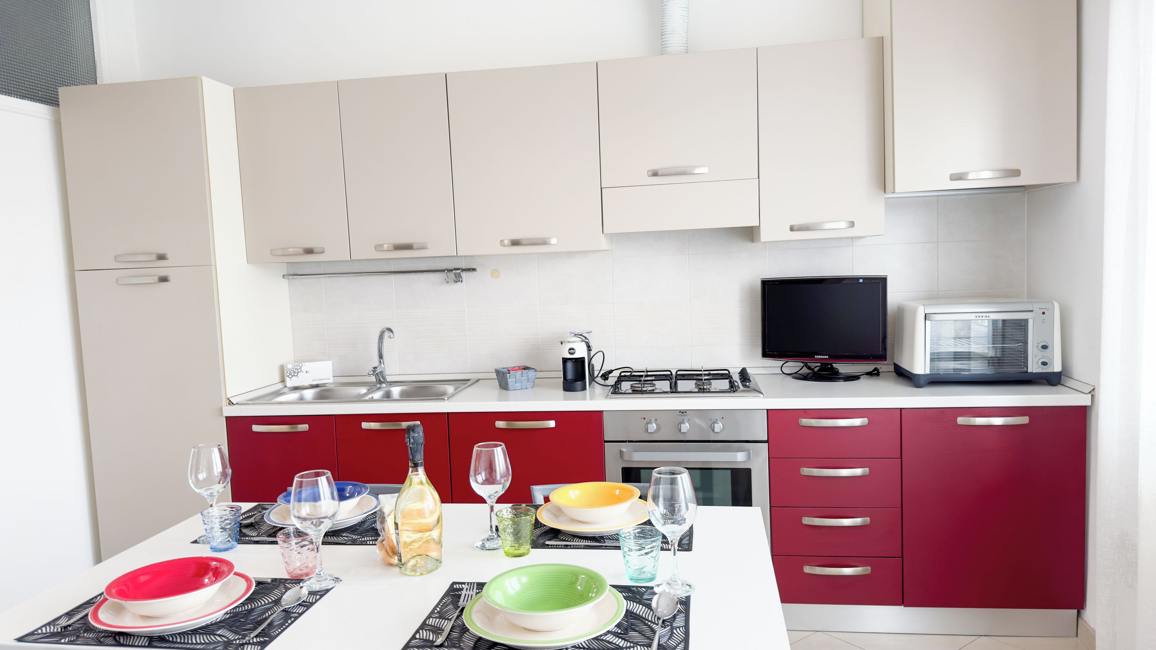 Uma cozinha moderna com uma mesa de jantar posta para dois, fogão a gás, micro-ondas e uma pequena televisão.