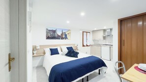 Quarto de hotel com cama, pequeno espaço de cozinha, mesa de jantar e porta.
