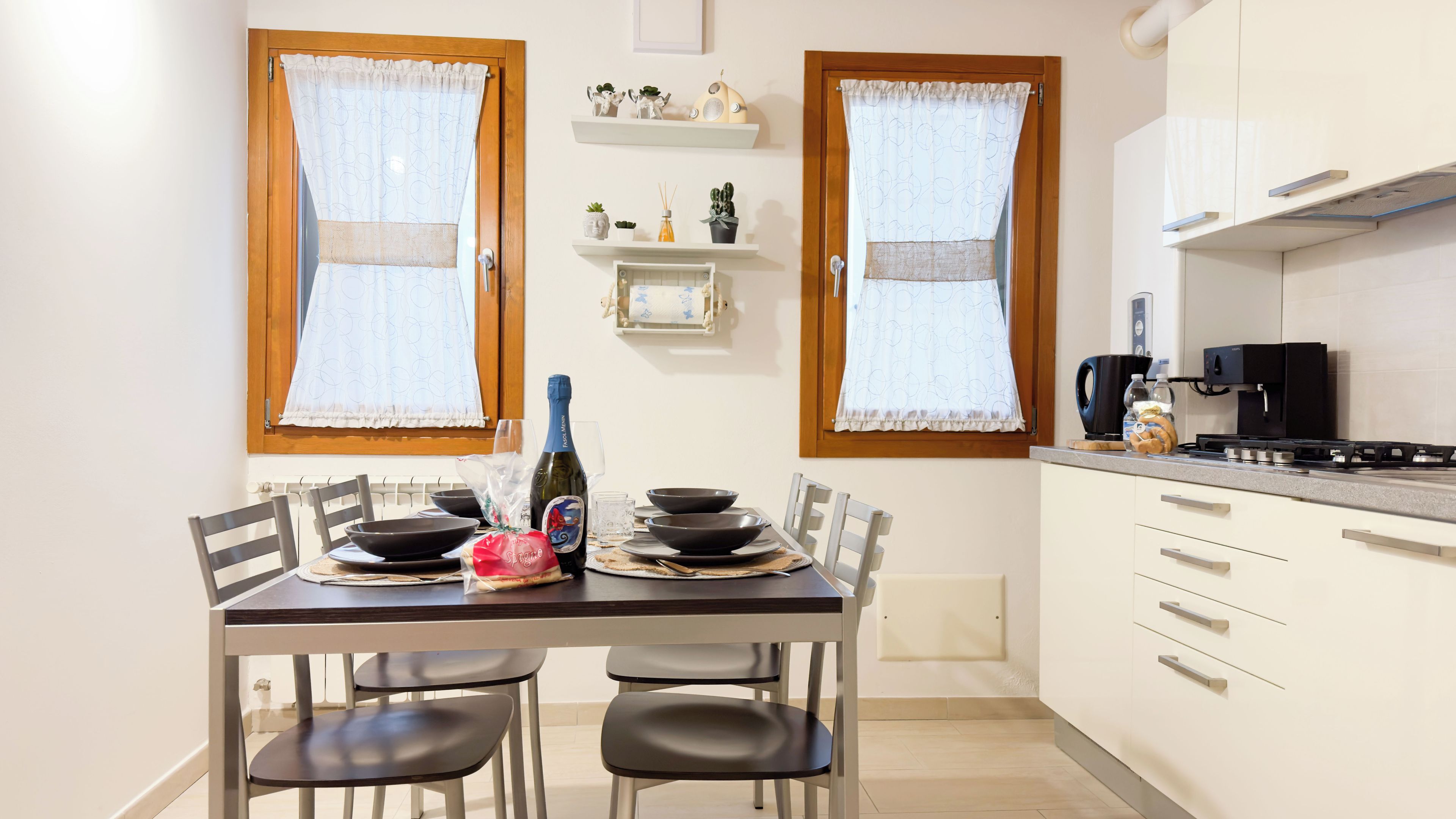 Uma sala de jantar com mesa posta para dois, uma garrafa de champanhe e um pacote de petiscos.