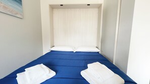 Uma cama de solteiro com colchão azul, almofadas brancas e duas toalhas brancas.