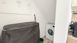 Uma lavanderia com máquina de lavar, uma peça coberta e um varal fixado na parede.