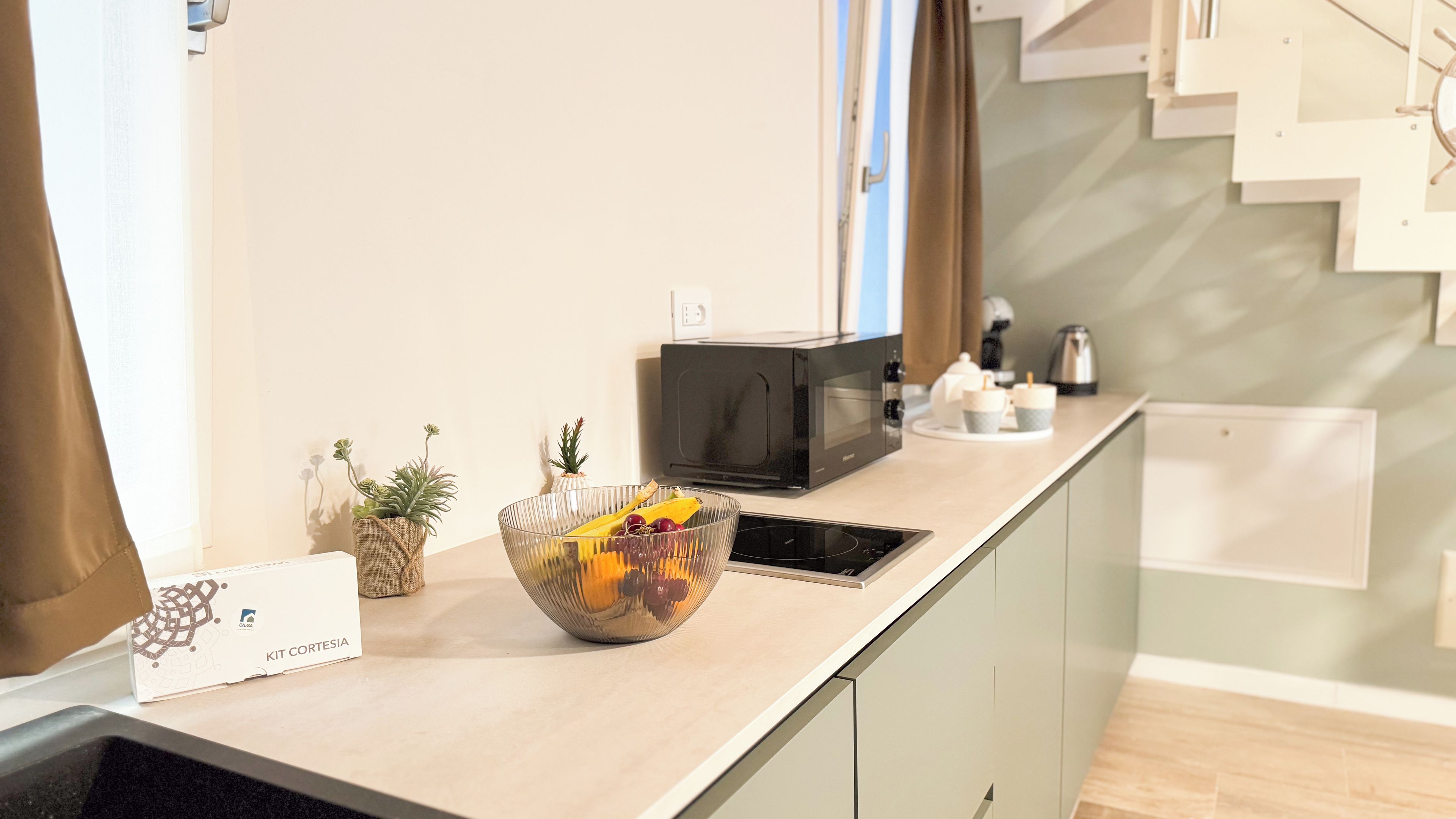 Cozinha moderna com micro-ondas, uma tigela de frutas e cafeteira.