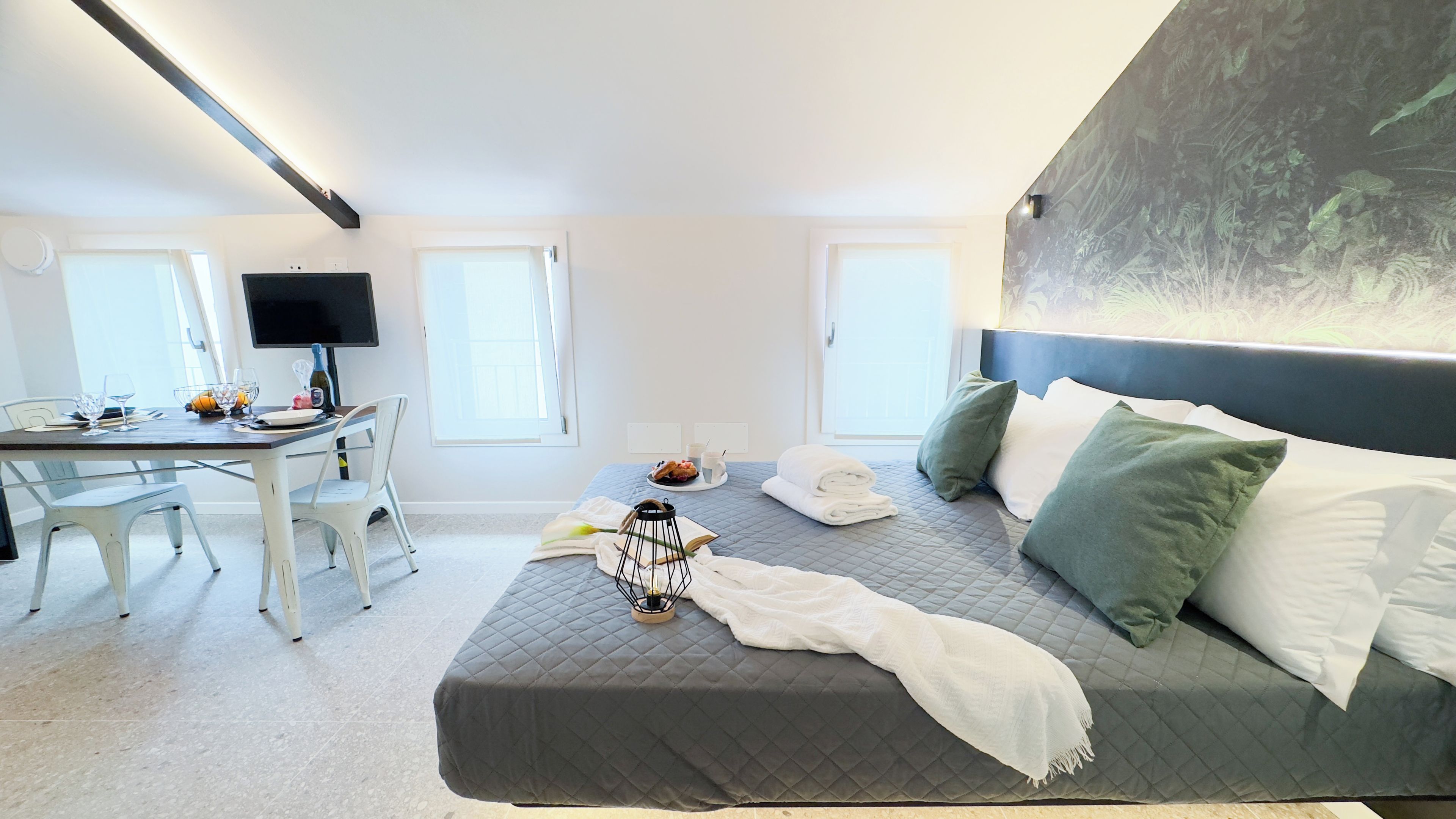 Quarto de hotel com cama, escrivaninha e computador, além de uma janela.