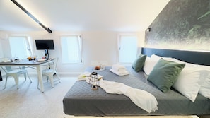 Quarto de hotel com cama, escrivaninha e computador, além de uma janela.