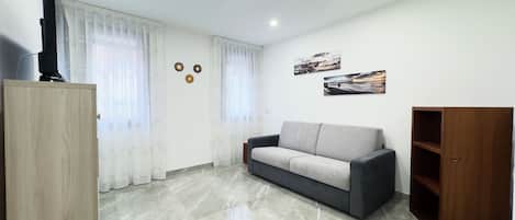 Uma sala de estar com um sofá, uma televisão sobre um móvel e um armário de madeira.