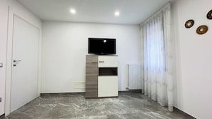 Uma sala de estar moderna com uma TV de tela plana fixada em um móvel, um radiador e uma janela com cortinas leves.