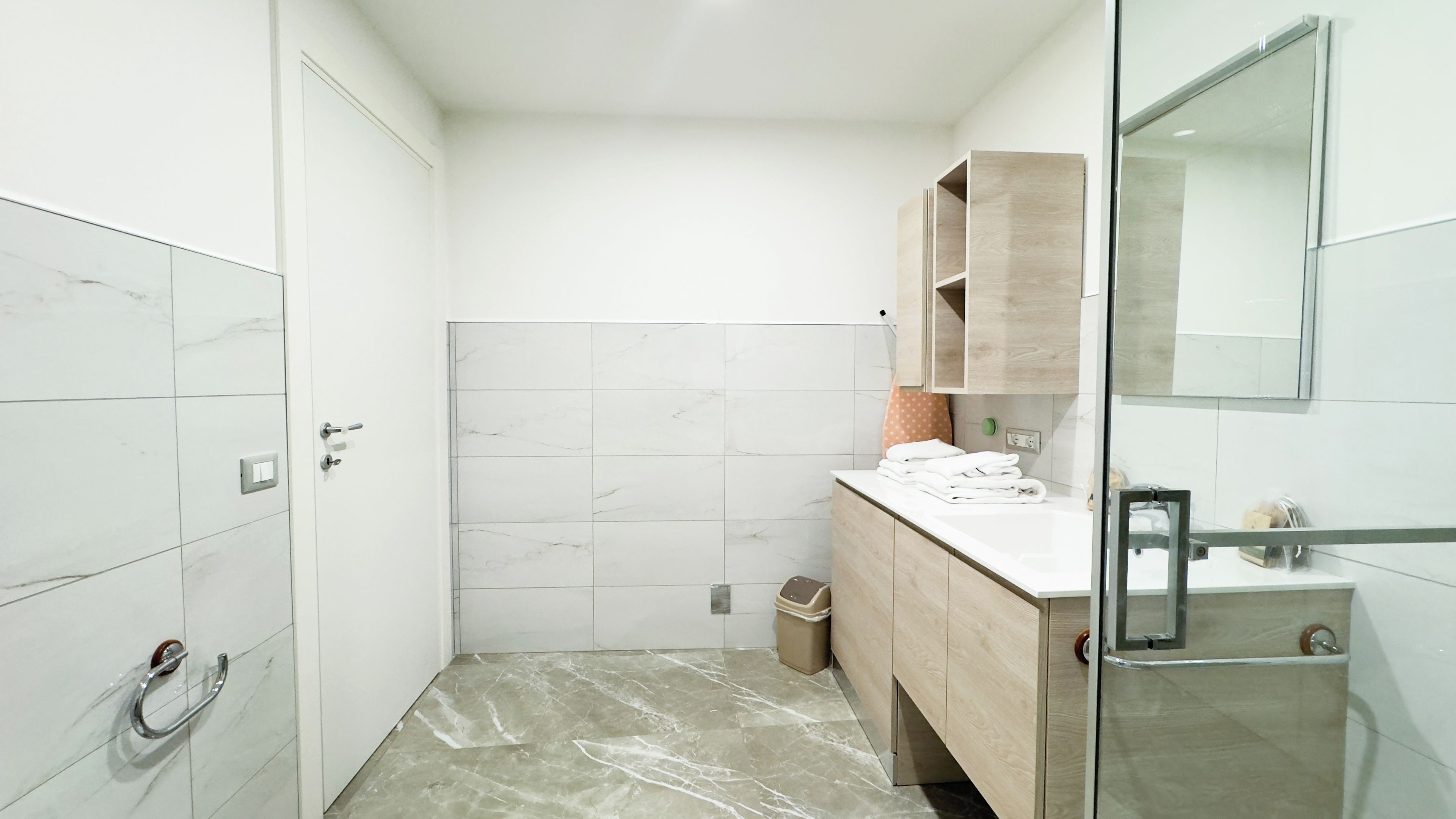 Um banheiro moderno com box de vidro, piso de mármore e toucador de madeira com espelho.