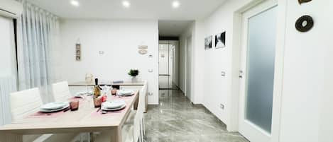 Uma área de refeições com uma mesa posta para quatro pessoas, uma planta em vaso e um letreiro com a palavra 'WELCOME' na parede.