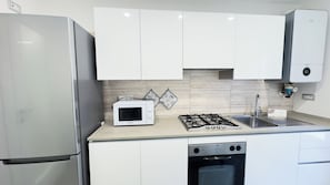 Cozinha moderna com armários brancos, geladeira de aço inoxidável, micro-ondas, fogão a gás e lava-louças.
