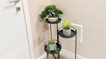 Suporte de plantas em metal preto com três níveis, com vasos de plantas em frente a uma parede.