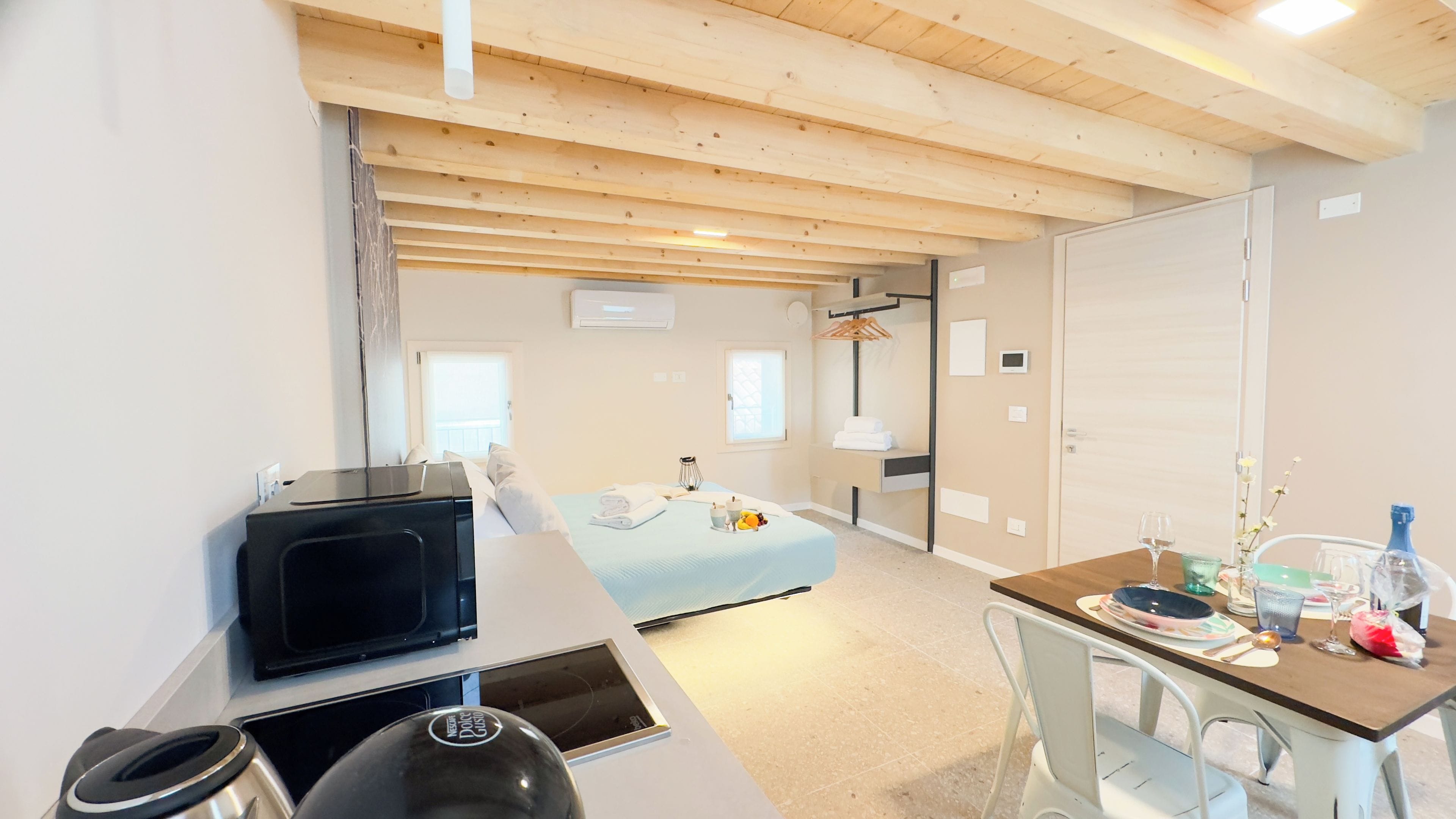 Quarto de hotel com cama, escrivaninha com computador, micro-ondas e área de jantar com mesa posta para dois.