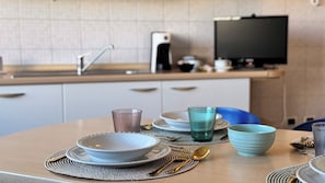 Uma cozinha moderna com uma mesa de jantar posta para dois, apresentando uma TV de tela plana, uma cafeteira e um revestimento de azulejos.