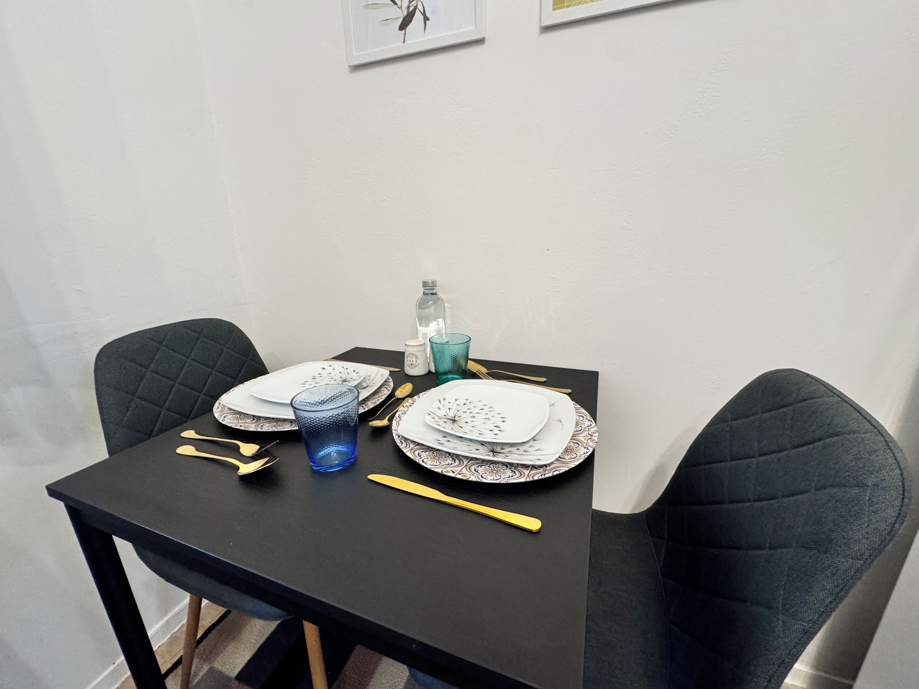 Mesa posta com pratos, talheres, um copo azul e uma garrafa de água.