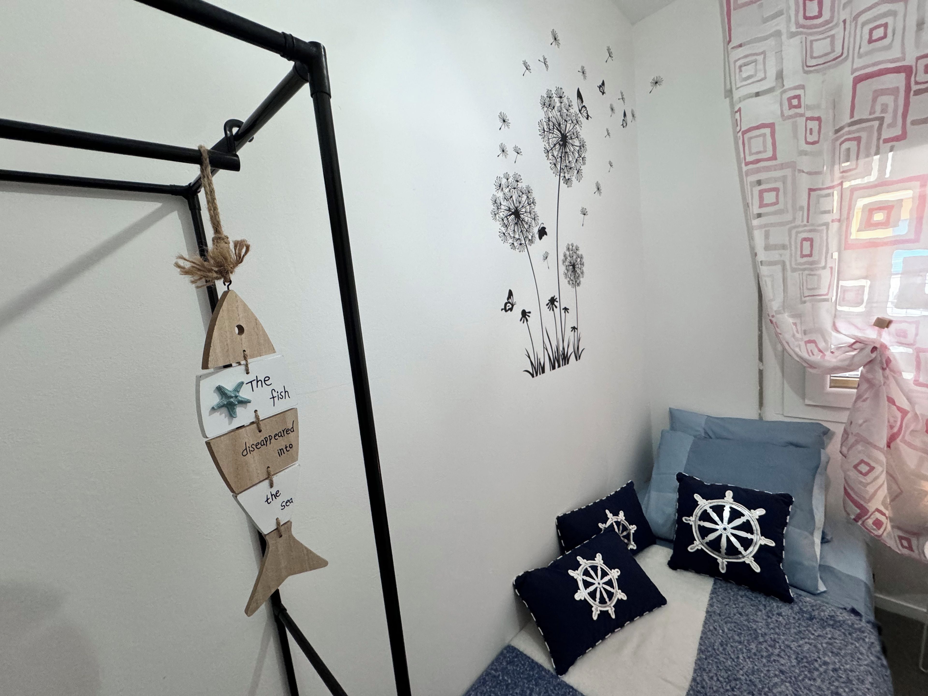 Quarto com cama, almofadas, um adorno na parede e um objeto pendurado.