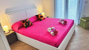 Uma cama com um edredom rosa vibrante, cabeceira branca e uma mesa de cabeceira com abajur.