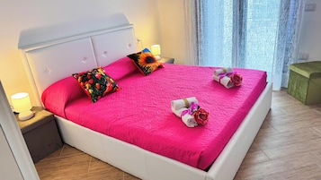 Uma cama com um edredom rosa vibrante, cabeceira branca e uma mesa de cabeceira com abajur.