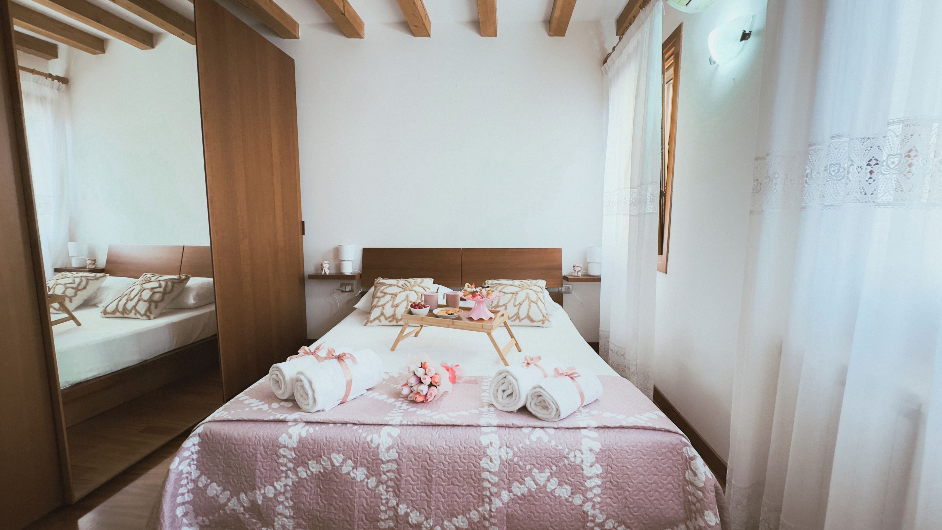 Quarto de hotel com cama, mesa de cabeceira, espelho e janela com cortinas.