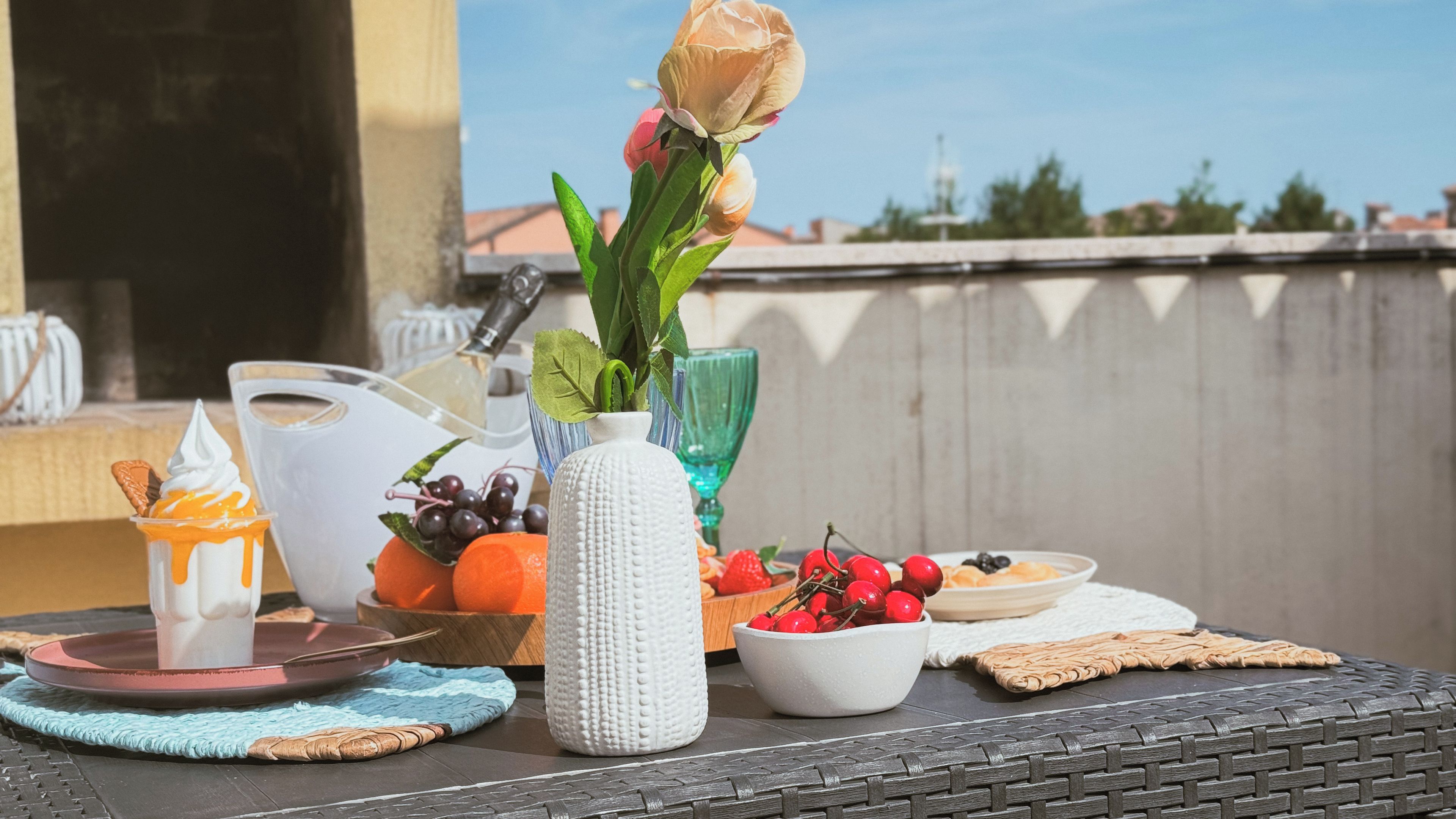 Uma mesa com diversos alimentos, um vaso de flores e um copo de bebida.