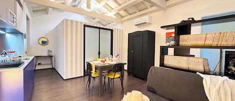 Uma cozinha moderna com fogão embutido, área de refeições com mesa e cadeiras, um armário preto e uma estante com livros.