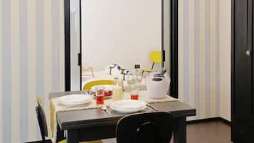 Uma sala de jantar com mesa posta para quatro pessoas, papel de parede listrado e uma porta preta.