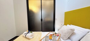 Quarto de hotel com uma cama, mesa de cabeceira com bandeja de café da manhã, uma toalha e uma porta com painéis de vidro jateado.