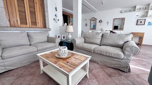 Uma sala de estar com dois sofás cinzas, uma mesa de centro branca e uma porta de madeira com persianas.
