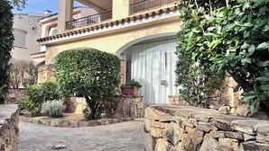 Um pátio com muro de pedra, planta em vaso e um edifício com porta branca e varanda.